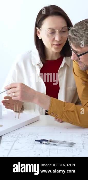 Two architects collaborate over blueprints and a white scale model ...