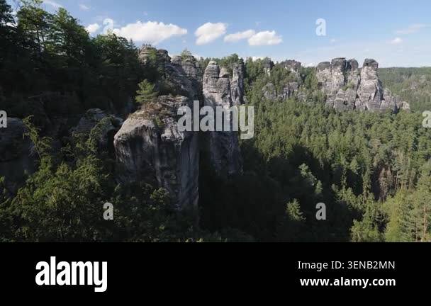 Sandstone cliff wall and rock towers rise above dense green forest in a ...
