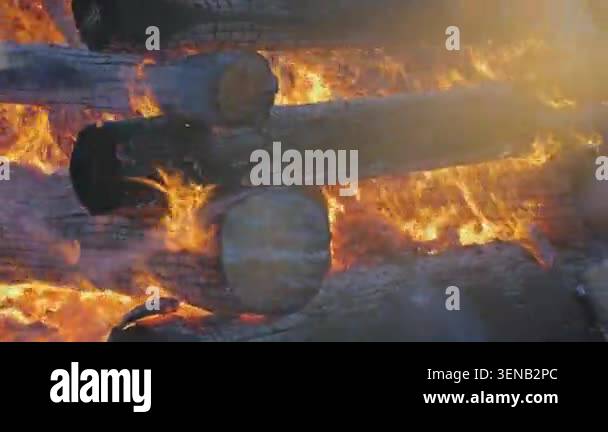 Backlit burning logs show flames, smoke, glowing embers, and warm ...