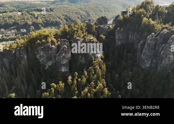 Sunlit sandstone cliff towers stand above a dense green forest valley ...