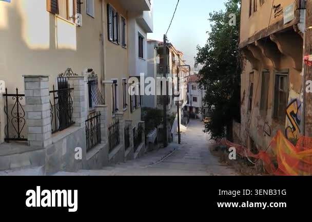 A narrow paved street descends between residential buildings, stone ...