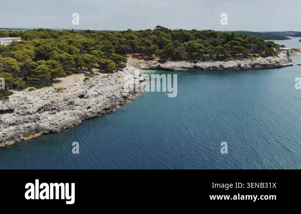 An aerial view shows a rocky coastline with clear turquoise water, a ...