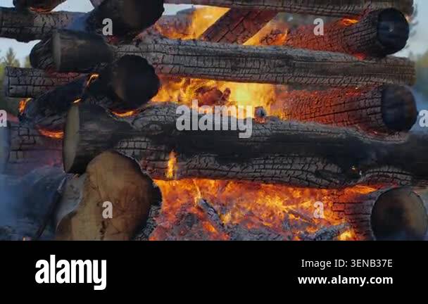Close view of stacked burning logs with bright flames, smoke, ash, and ...