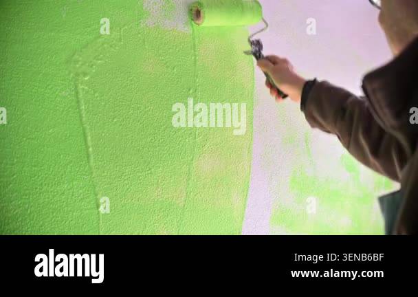 Person applying bright green paint to an interior textured wall using a ...