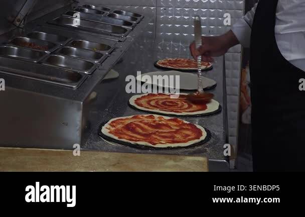 Chef spreading fresh tomato sauce on pizza dough base with a ladle ...