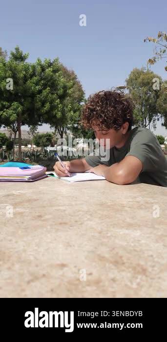 Thoughtful teenage boy doing homework outdoors in a sunny park. Student ...
