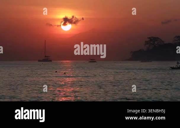 Time-lapse of a vivid red sunset over the sea and coast with yachts on ...
