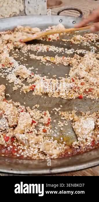 Chef stirs golden rice with meat and vegetables in huge paella pan ...