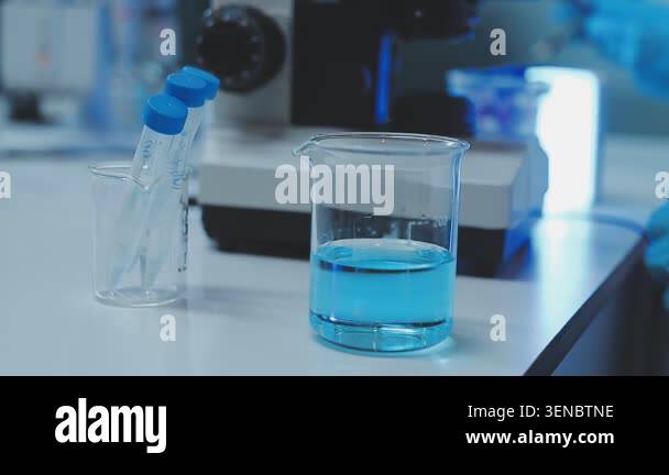 scientist in a blue suit and gloves holds a test tube with a liquid in ...