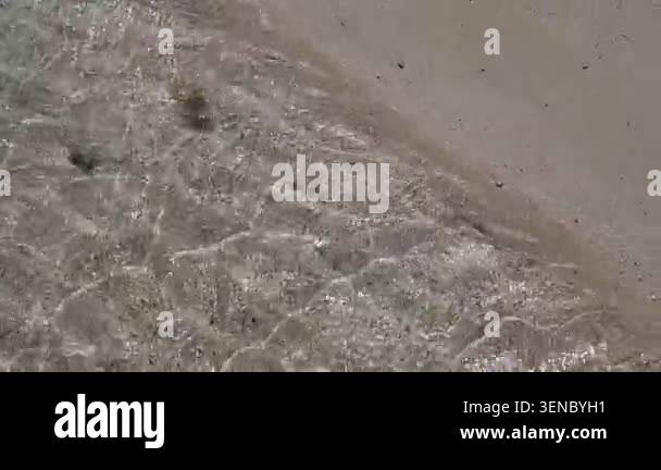 Calm transparent sea water with sun glare gently washing over a ...