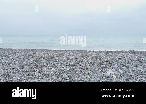 Cold and calm sea waves washing a deserted pebble beach shore under a ...