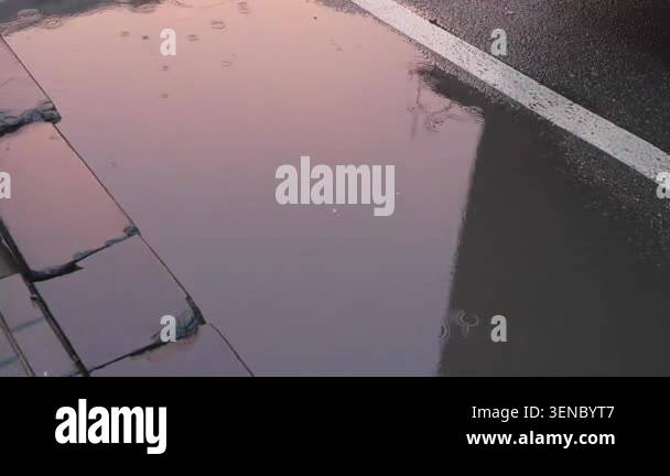 Raindrops creating ripples in a puddle on an urban street at dusk ...