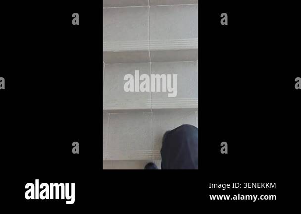 A vertical video capturing a person feet walking up a flight of stairs ...