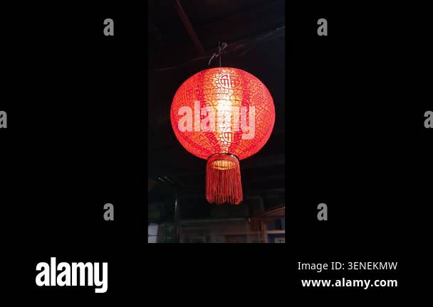 A vertical shot of a large, round red Chinese lantern illuminated and ...