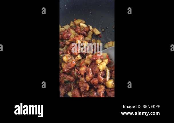 A close-up shot of a spatula stirring pieces of chicken and potatoes in ...