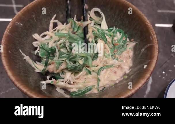 A horizontal close up video of chopsticks mixing green vegetables and ...
