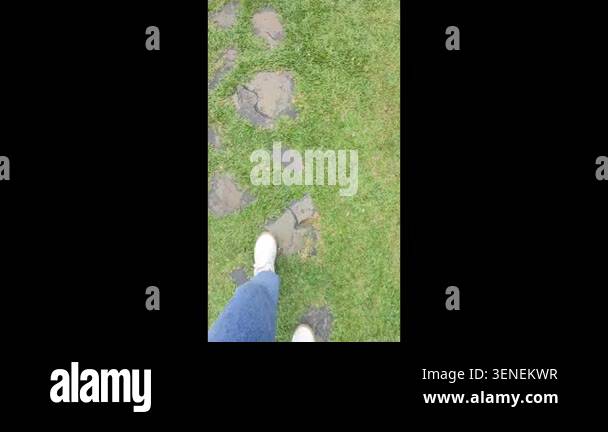 A vertical POV shot of feet in white sneakers walking on a stone path ...