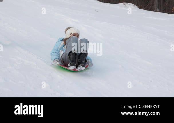Front view of young girl smiling, tobogganing down snowy hill. Happy ...