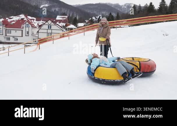 Side view of two cute female kids lifting their yellow snow tubes on ...