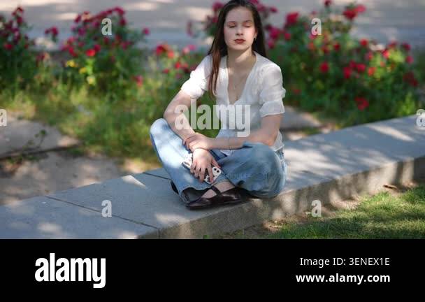 Beautiful young pensive woman sitting cross-legged on a concrete ledge ...