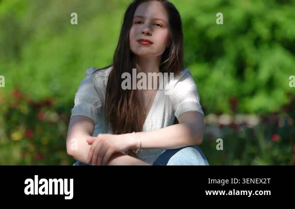 Portrait of a beautiful young woman with long hair sitting in a park ...