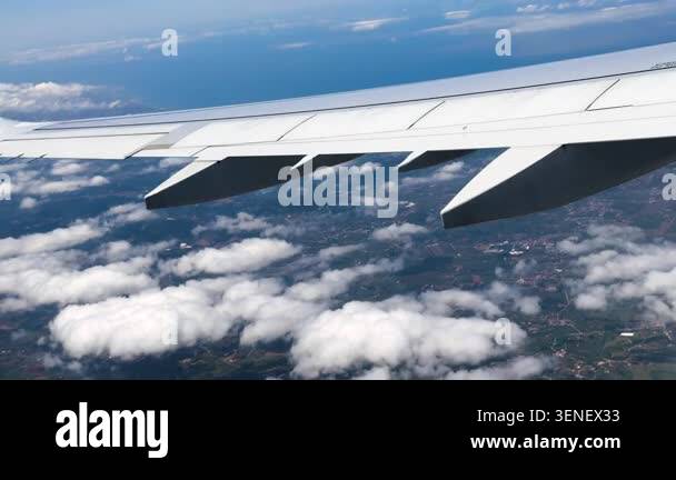 Airplane wing extends above scattered clouds and distant landscape ...