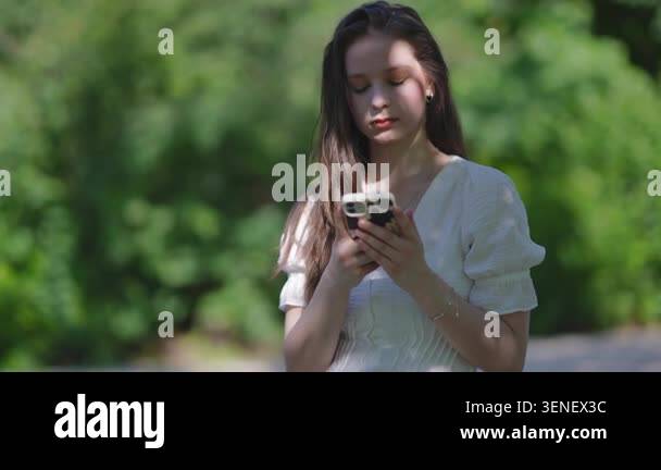 Young woman standing in a park, completely focused on texting on her ...