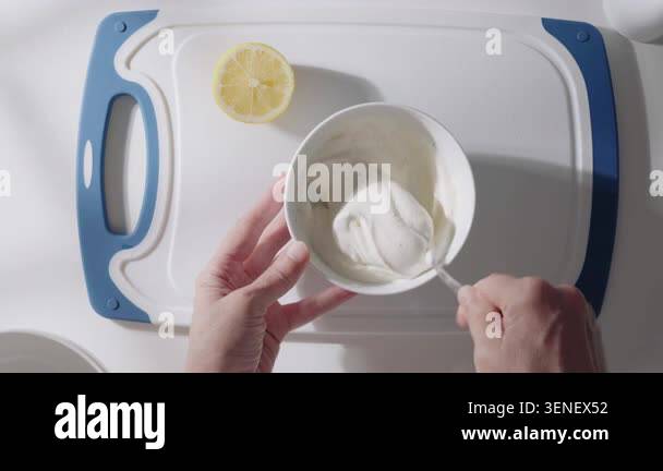 Hands stir creamy Greek yogurt sauce in a bowl beside a lemon on a ...