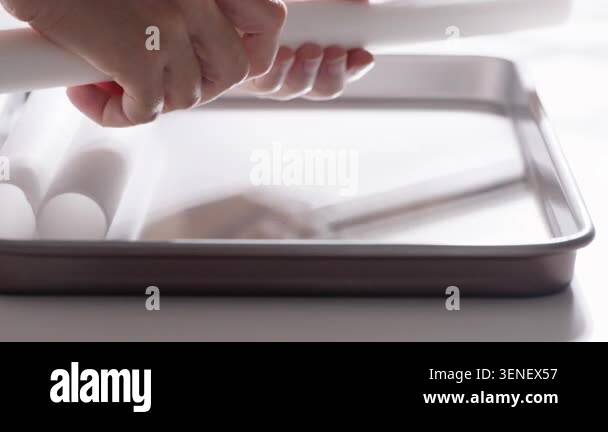 Hand lines a baking tray with parchment paper during food preparation ...