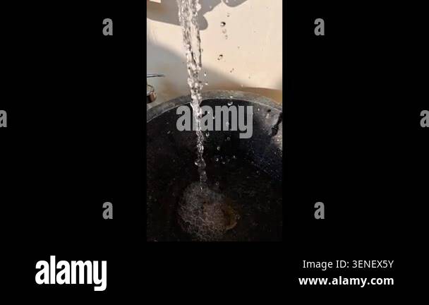 A vertical shot of a stream of clear water pouring into a black bucket ...