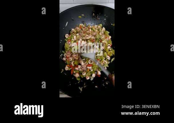 A close-up shot of squid and green chilies being stir-fried in a hot ...