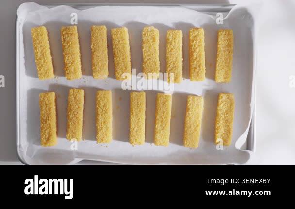 Hands arrange breaded fish sticks on a parchment lined baking tray ...