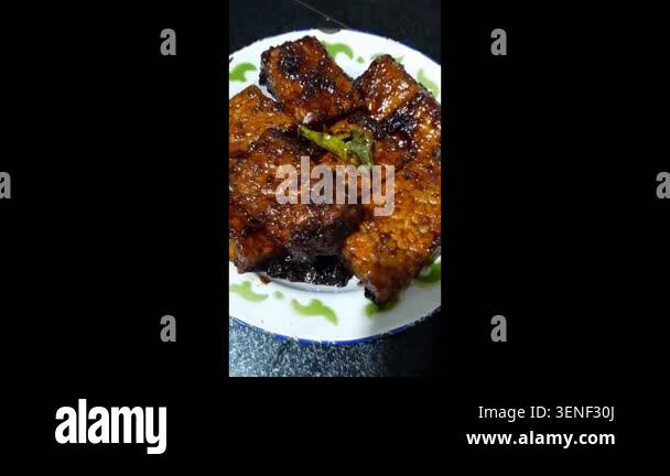 A close-up shot of crispy fried tempeh slices served with a fresh green ...