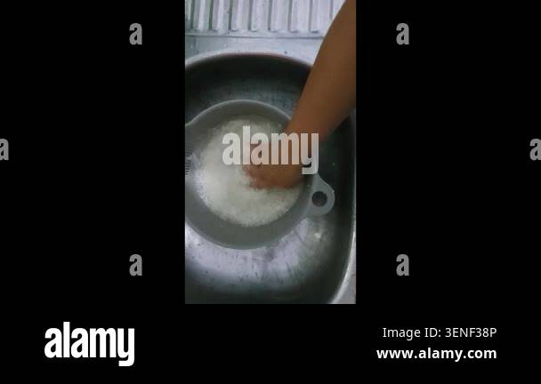 Close up of a hand washing raw rice in a gray plastic strainer bowl ...