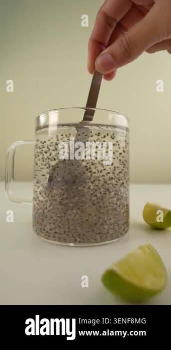 Woman hand stirring chia seeds with a spoon in a glass cup of water ...