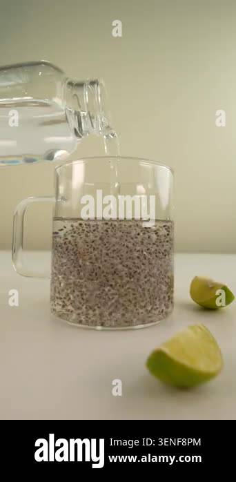 Fresh water pouring into a glass with chia seeds from a bottle on white ...