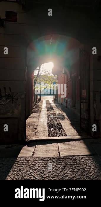 Ancient stone arch framing bright sunlight at end of narrow alley ...
