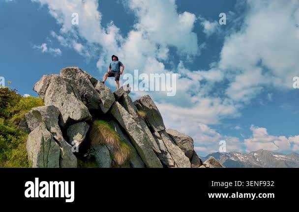 Lone traveler standing tall on rocky mountain summit gazing at alpine ...