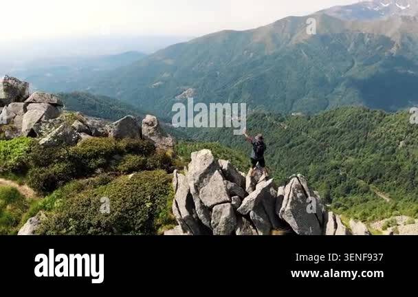 Man standing on large rocky mountain peak with arm raised in triumph ...