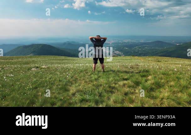Male hiker standing with arms raised wide on alpine narcissus meadow ...