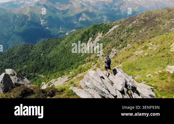 Male hiker navigating rocky alpine summit terrain with green mountain ...