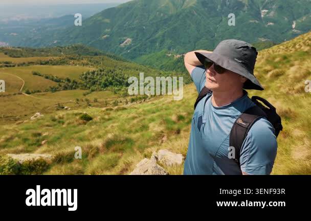 Close portrait of male hiker in wide brim sun hat and backpack walking ...
