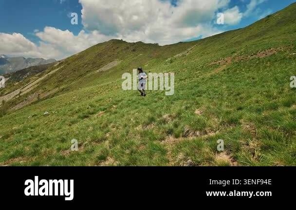 Lone traveler walking across expansive green alpine meadow with ...