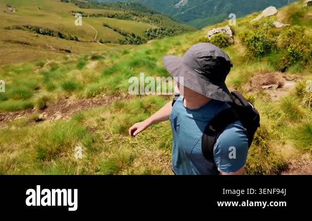 Male traveler in sun hat and backpack navigating rocky alpine trail ...