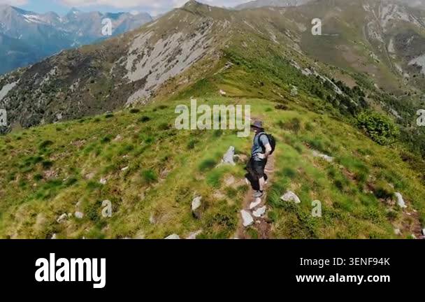 Drone shot of hiker descending steep rocky trail along dramatic alpine ...