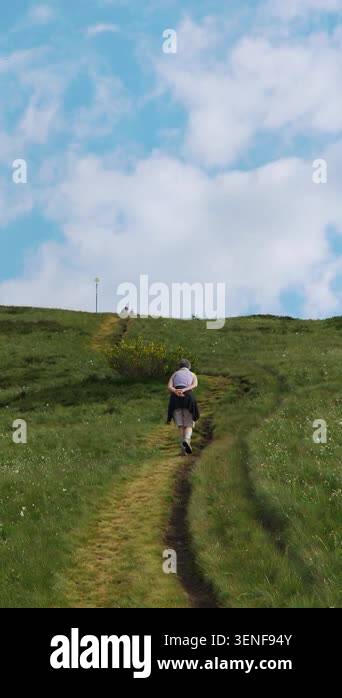 Single hiker walking along trail through open alpine meadow on sunny ...