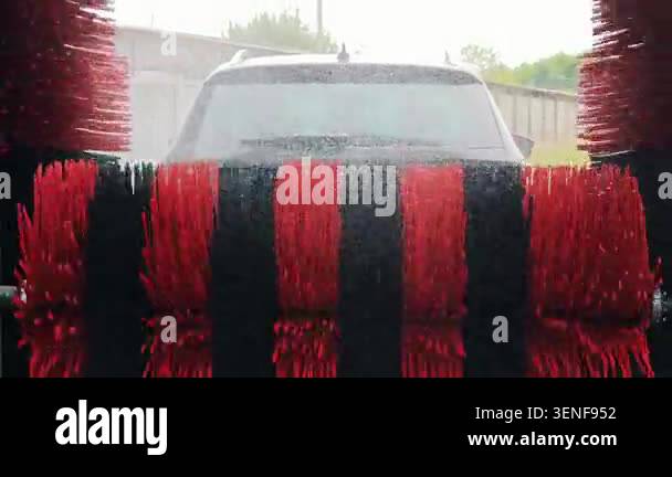Vehicle enveloped by large red and black rotating brushes in automatic ...