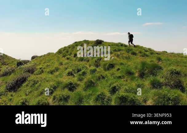 Drone shot of lone hiker standing on top of smooth green alpine hill ...