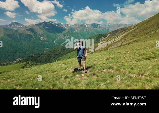 Male hiker drinking water from bottle while resting on green alpine ...