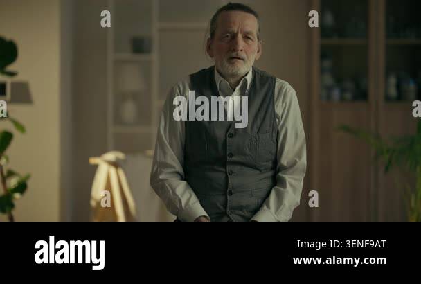 Older man sits facing the camera in a softly lit home interior with ...